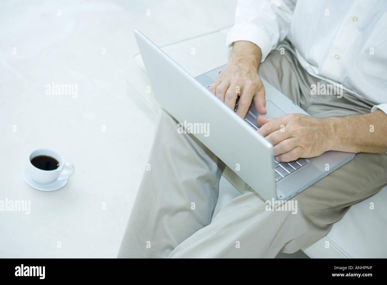 Man sitting using laptop computer, cup of coffee beside him, cropped ...
