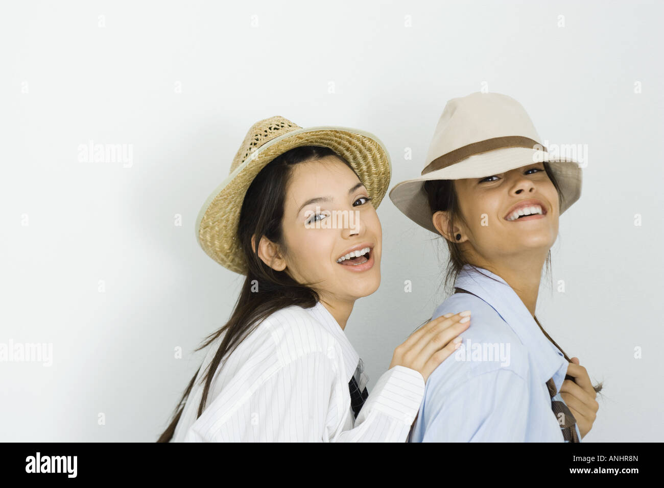 Two young female friends wearing hats and ties, smiling at camera, one ...