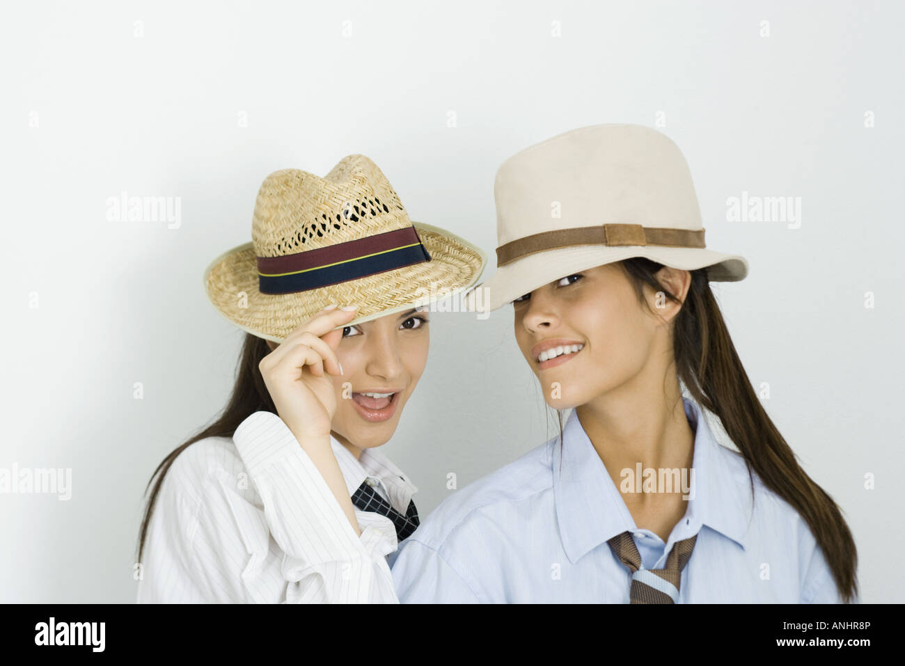 Two young female friends wearing hats and ties, both smiling at camera ...