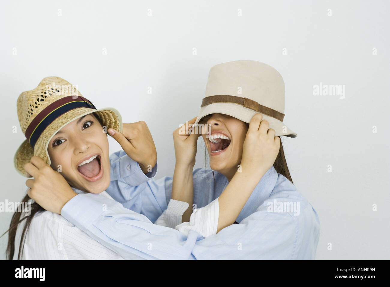 Two young friends pulling hats over each other's faces and smiling, one ...