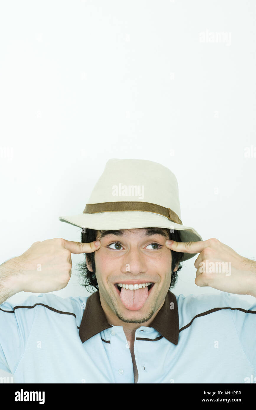 Young man wearing hat, sticking out tongue, pulling eyes to the side ...