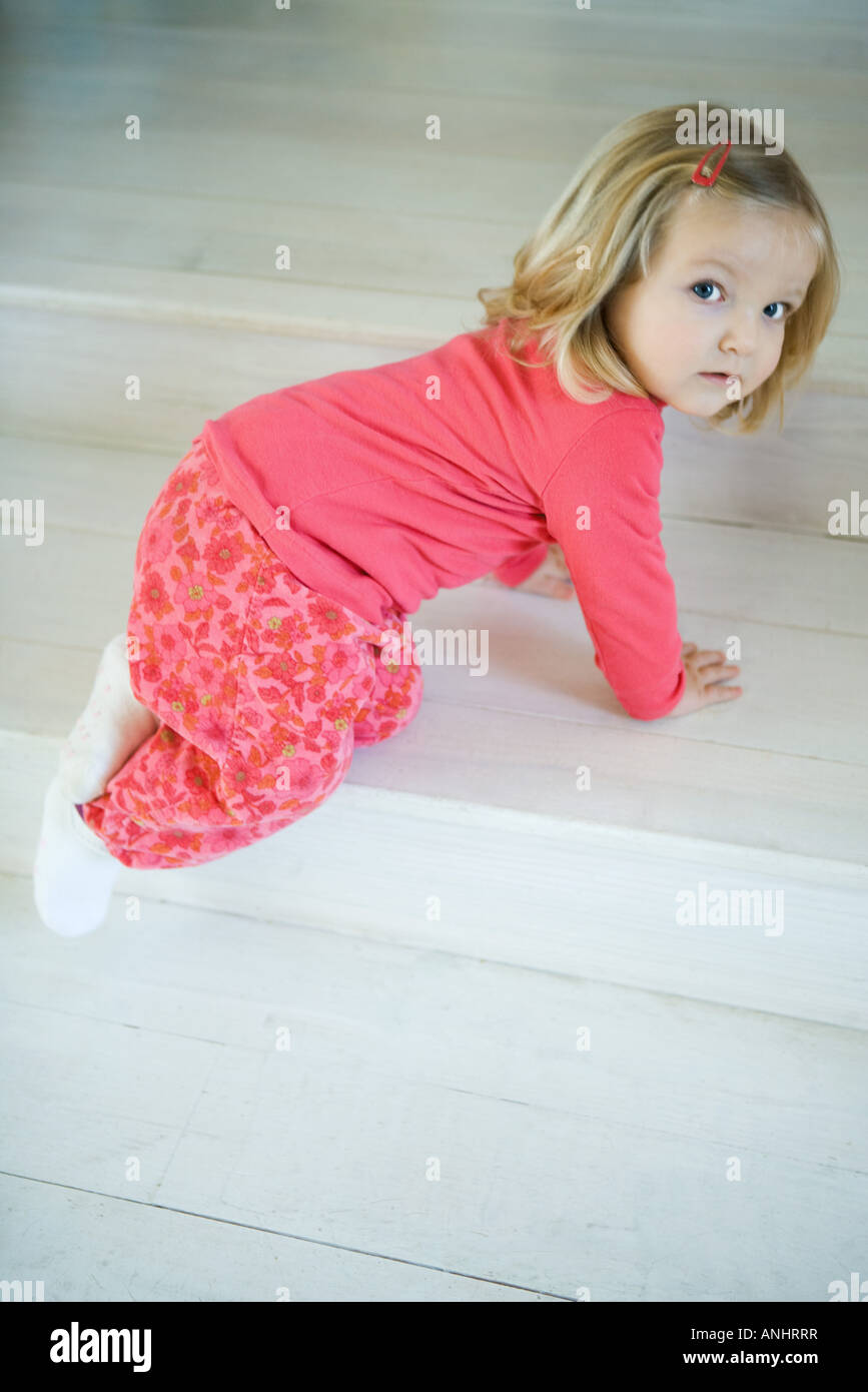 Blonde toddler girl crawling on steps, looking over shoulder at camera ...