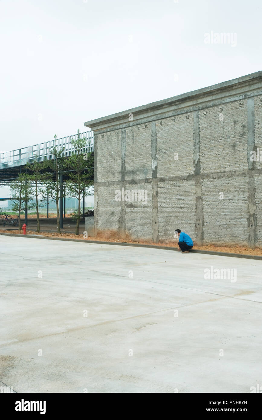 Urban scene, person crouching next to edge of building Stock Photo - Alamy