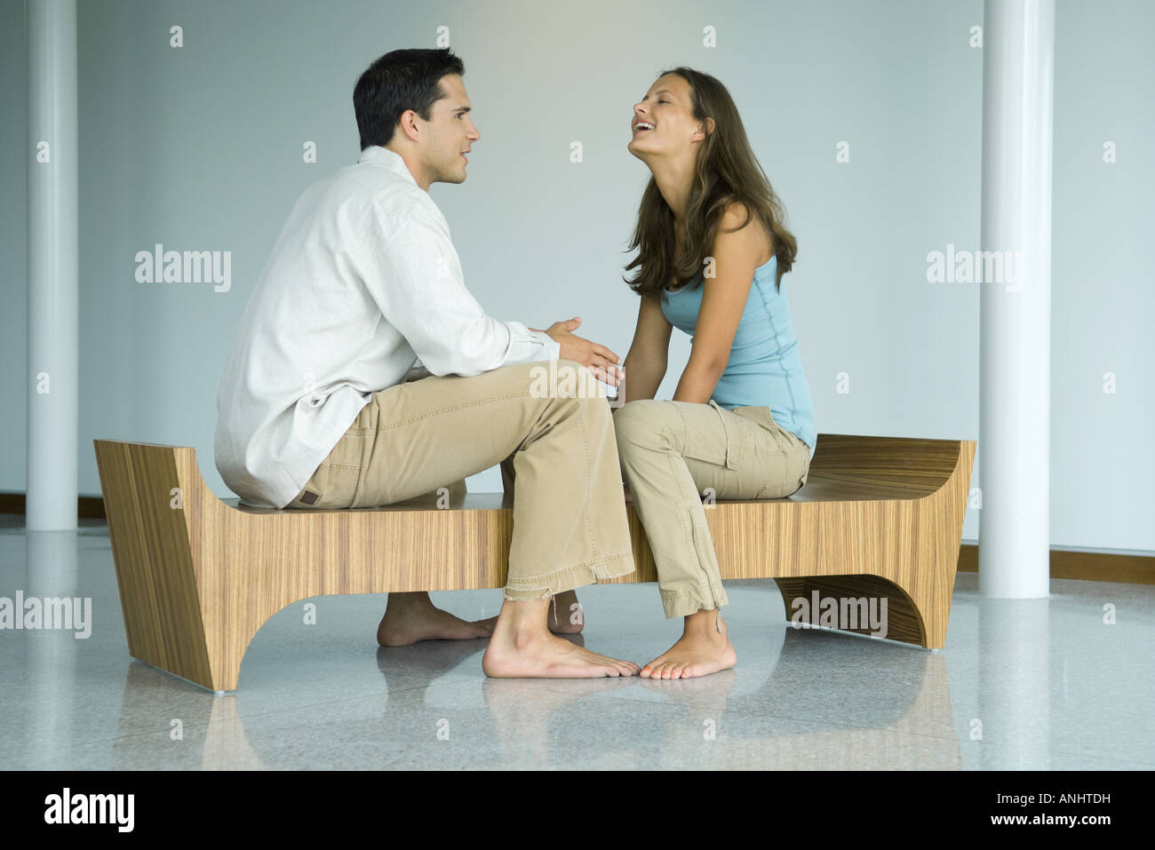 Young couple sitting face to face on bench, laughing together Stock ...