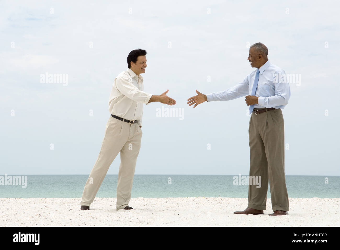 Two businessmen standing on the beach, reaching out to shake each other ...
