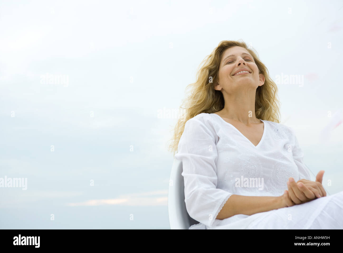 Woman sitting with eyes closed and head back, smiling, sky in ...