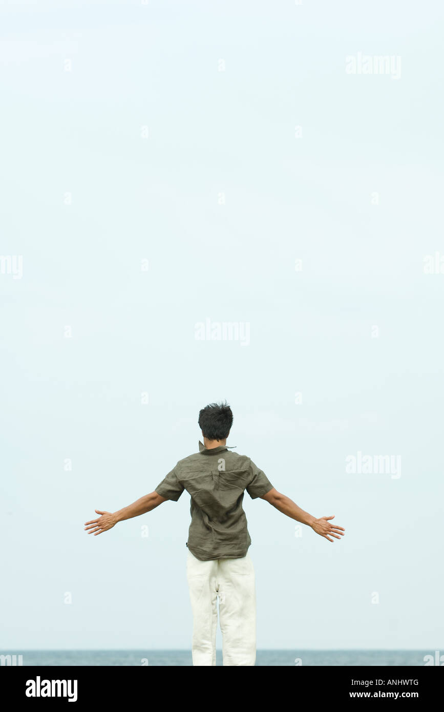 Man standing by sea with arms out, rear view Stock Photo - Alamy