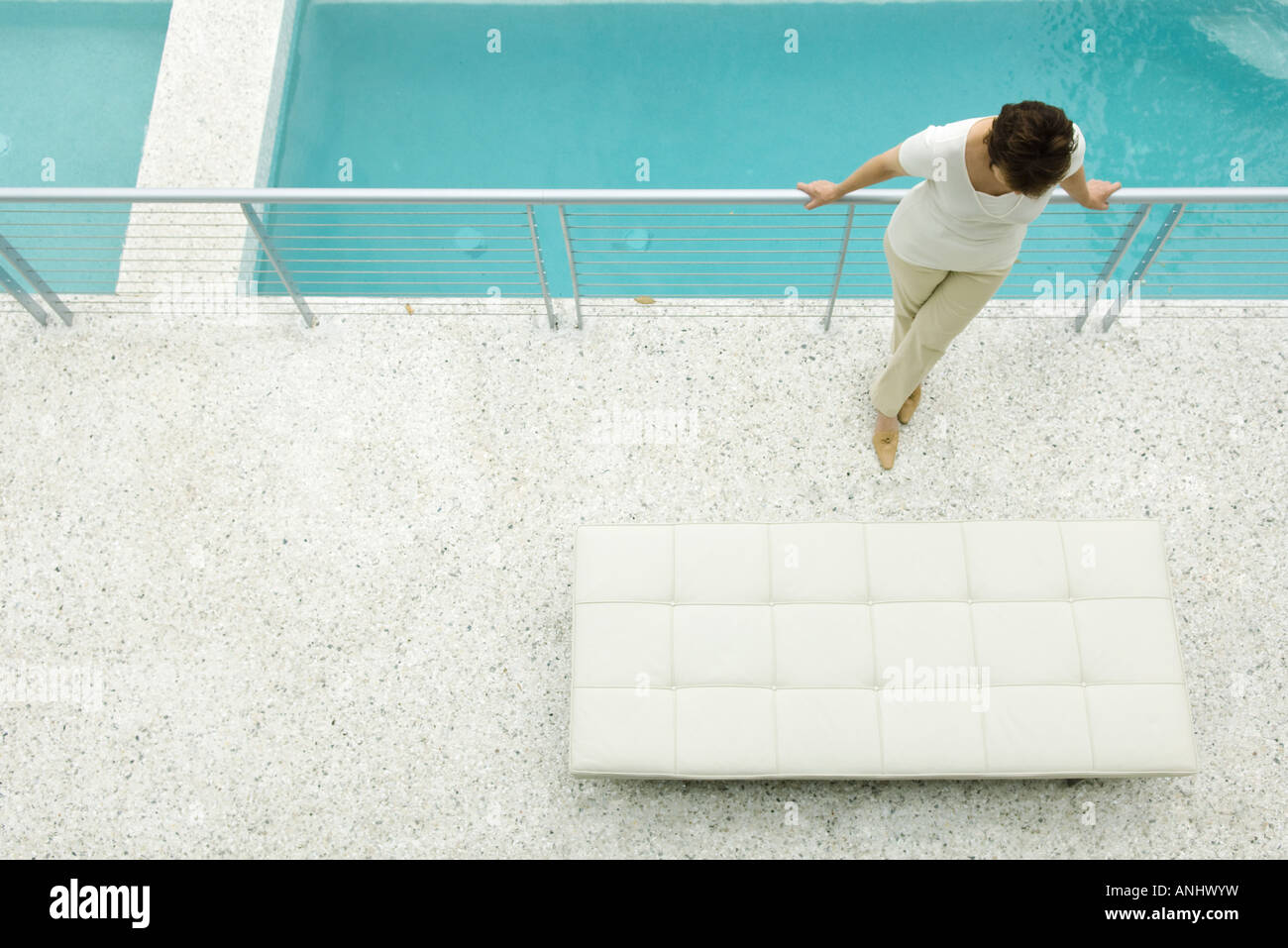 Woman standing on terrace, leaning against railing, swimming pool in ...