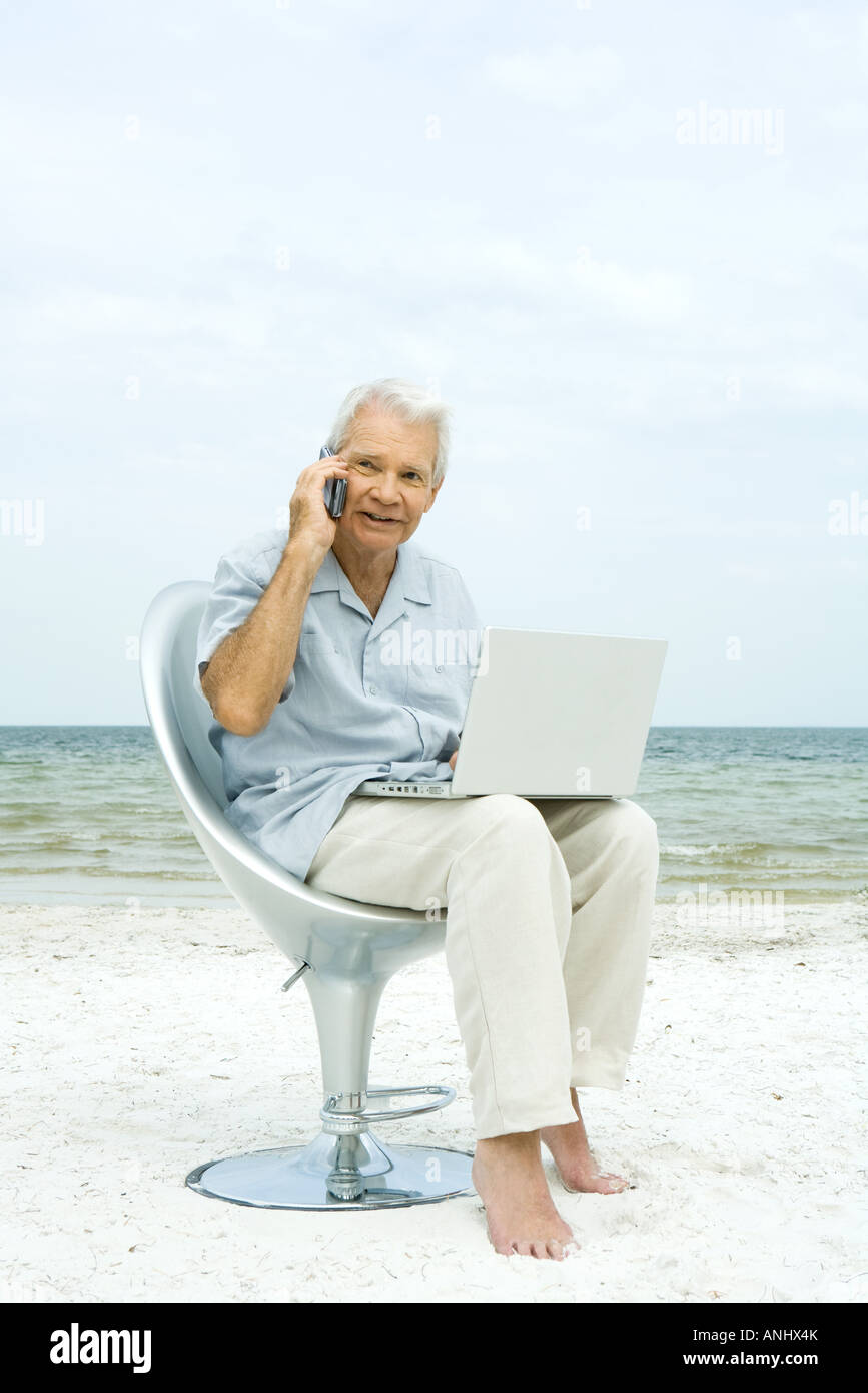 Senior man using laptop on beach, making phone call Stock Photo - Alamy
