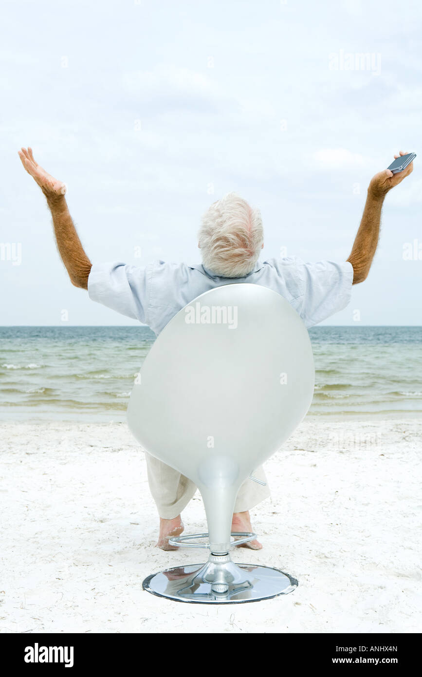 Senior man holding cell phone, arms up and head back, rear view Stock ...