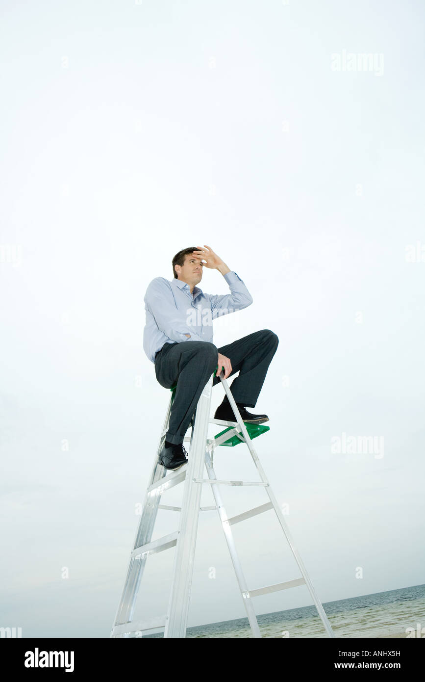 Man sitting on top of ladder, shading eyes, looking away Stock Photo ...