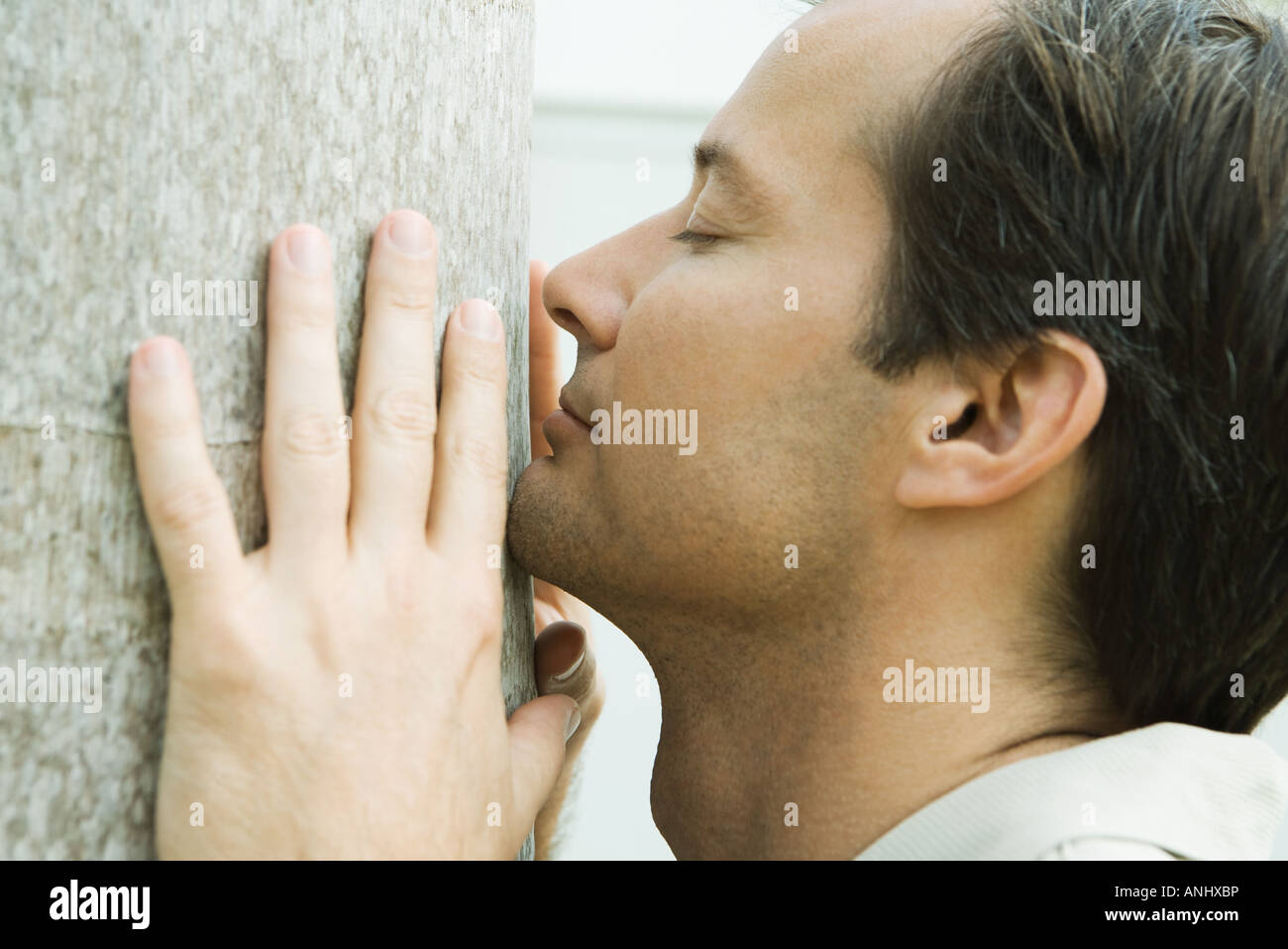 Man smelling tree trunk, eyes closed, side view, close-up Stock Photo ...