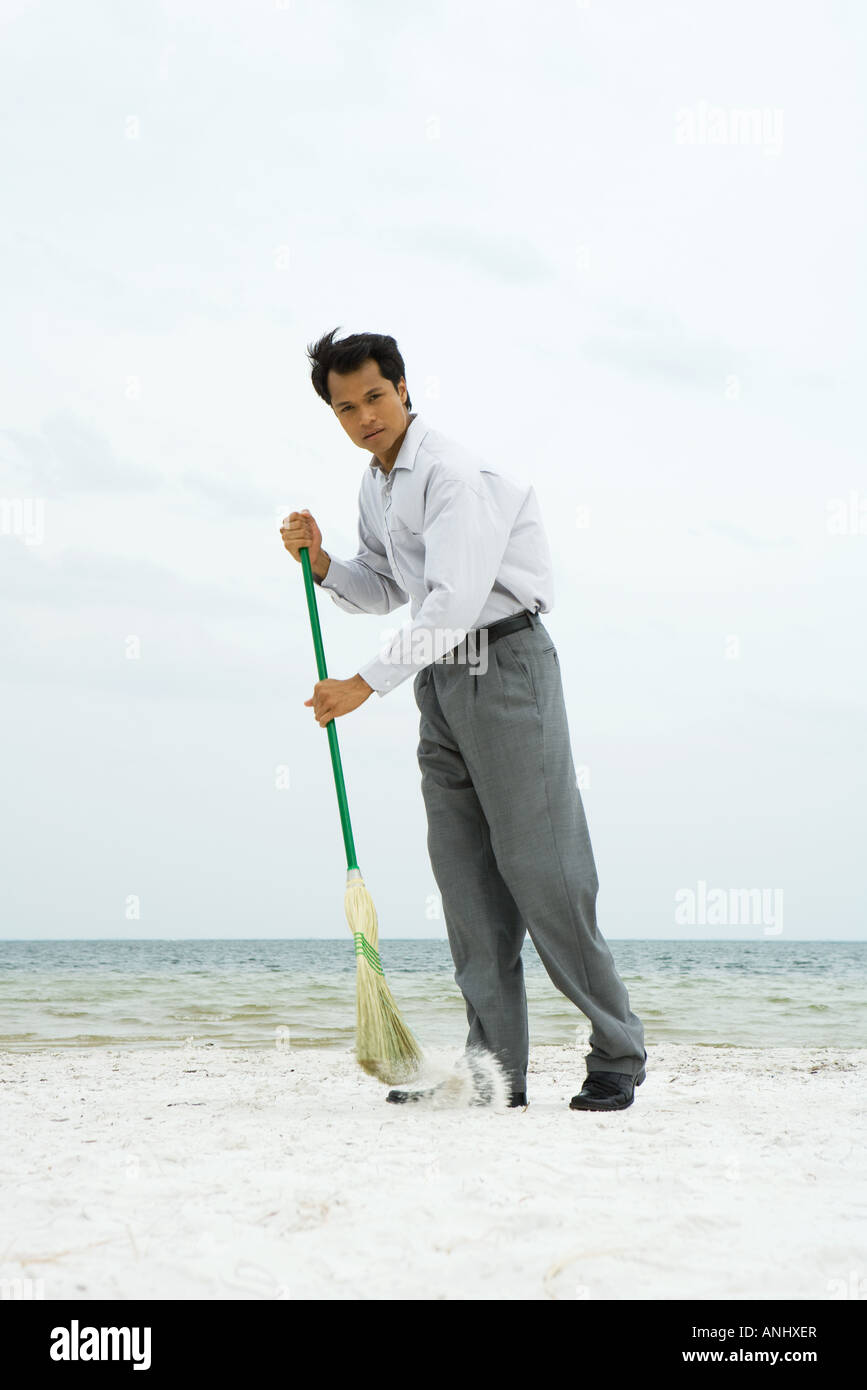 Man standing on beach sweeping with broom, looking at camera Stock ...
