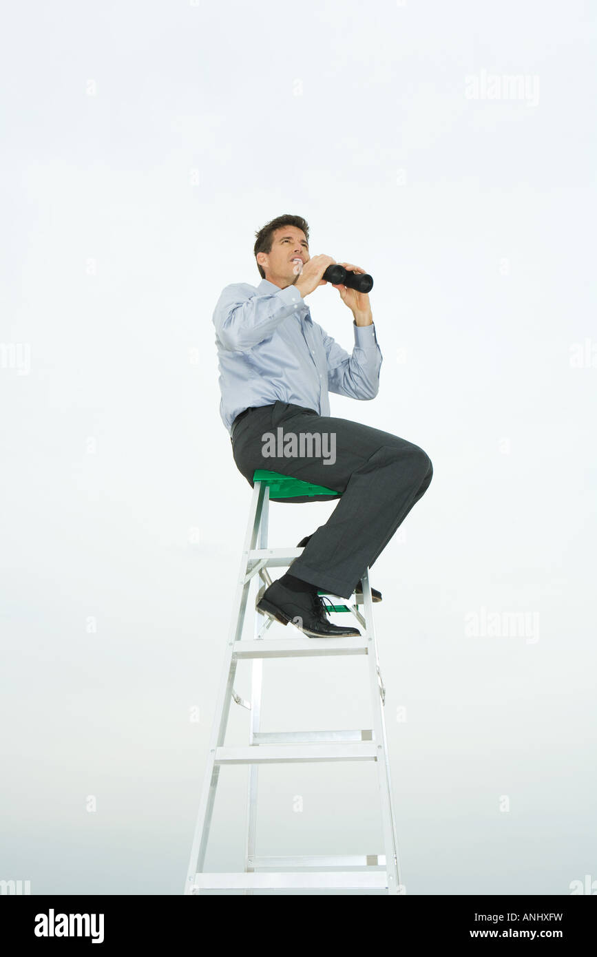 Man sitting on top of ladder, holding binoculars, looking up Stock ...