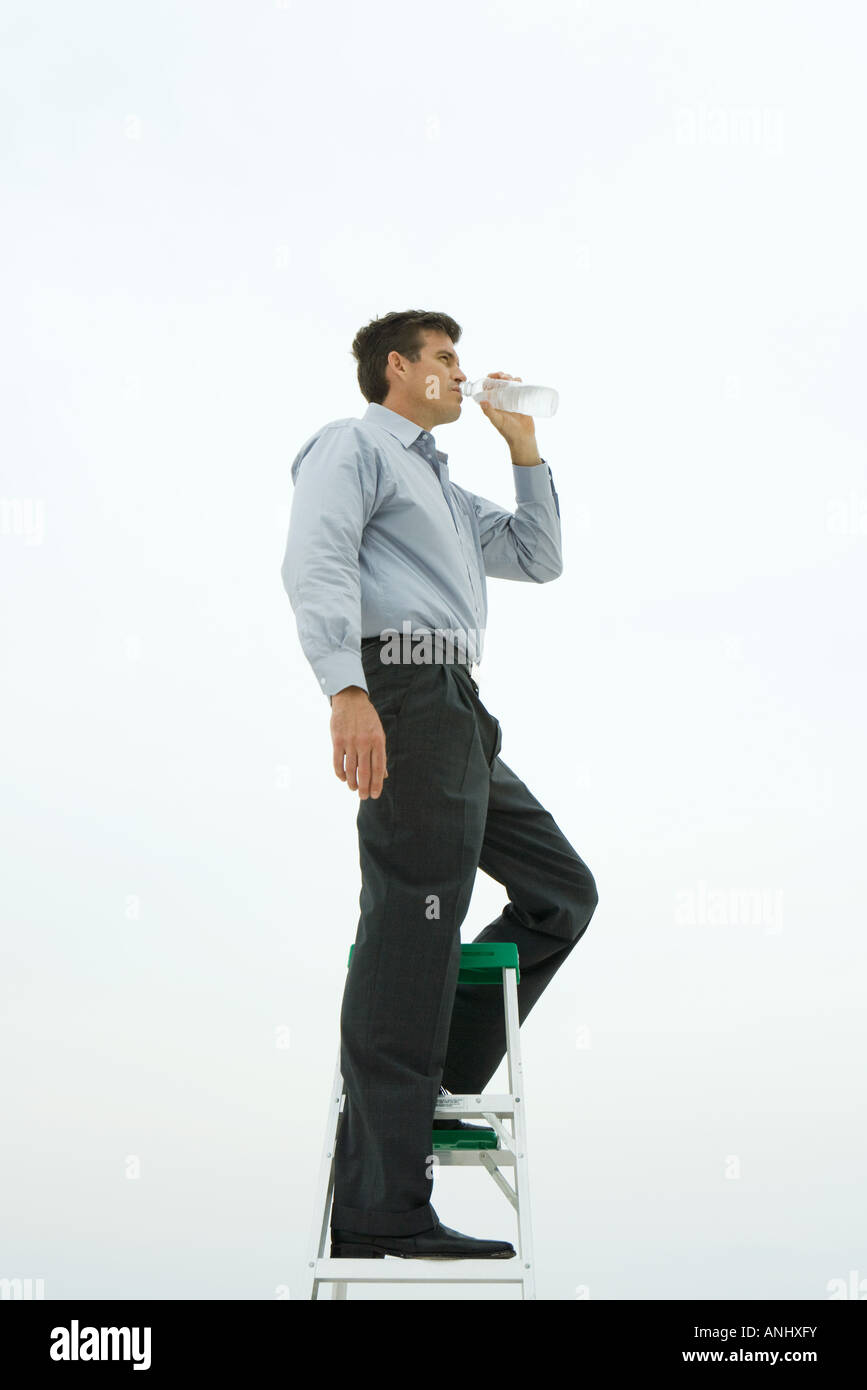 Man standing on top of ladder, drinking bottled water, side view Stock ...