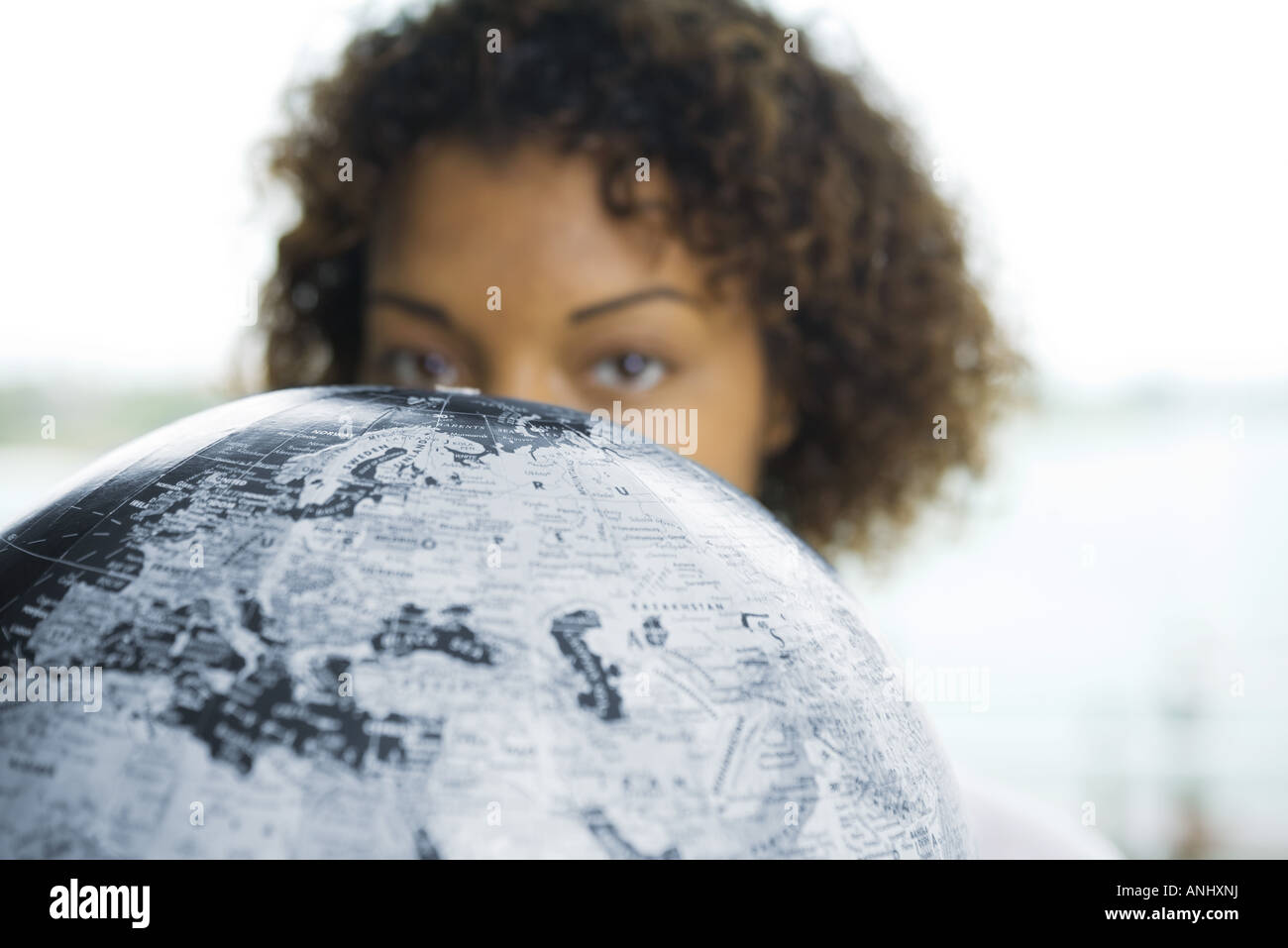 Woman looking over globe at camera, cropped view Stock Photo - Alamy