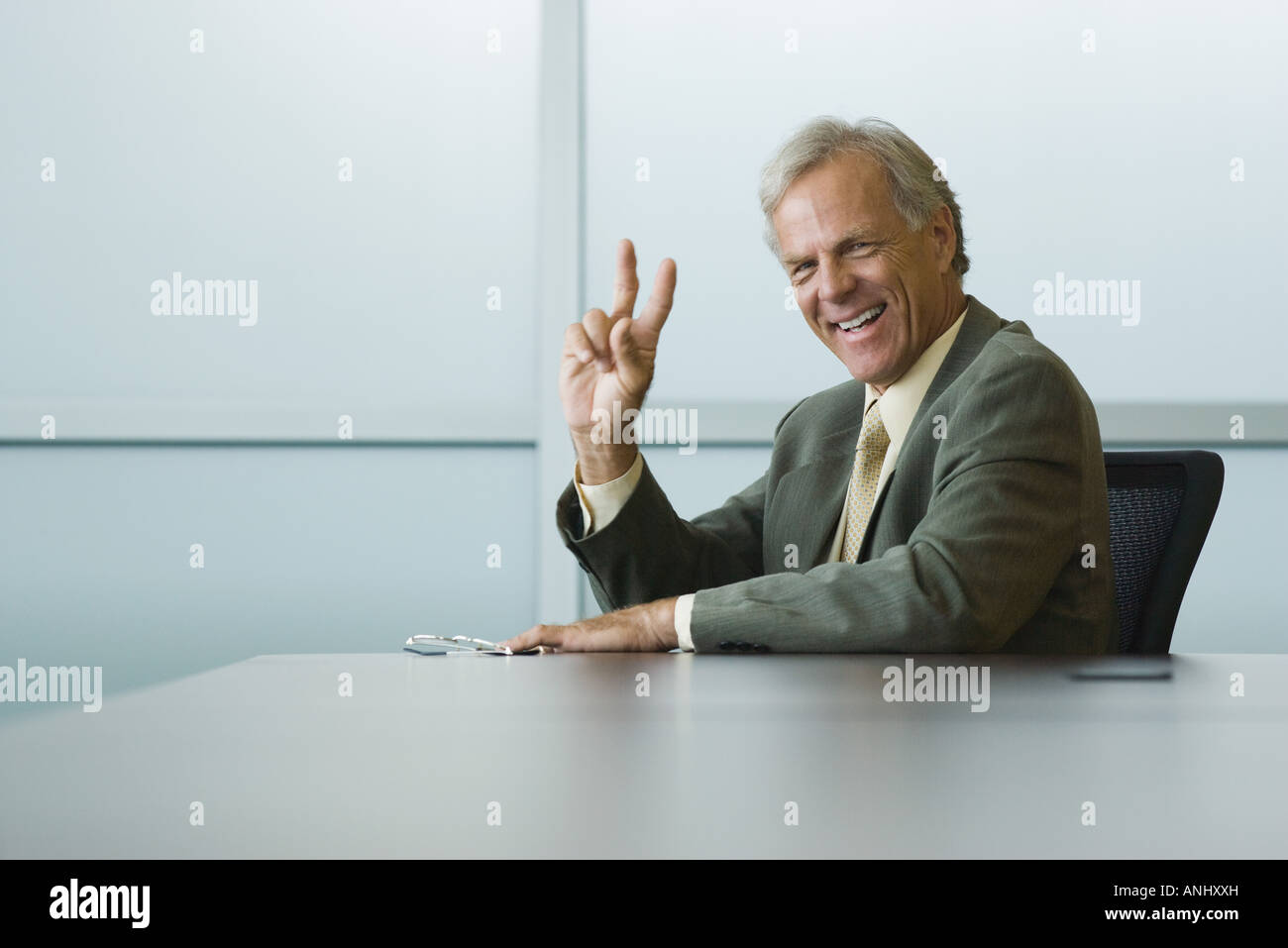 Businessman making peace sign, smiling at camera Stock Photo - Alamy