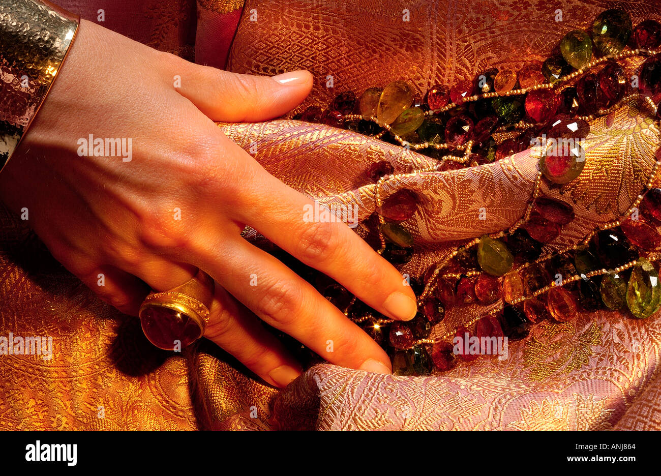 hand taking a string of gem stones against a gold embroidered material ...
