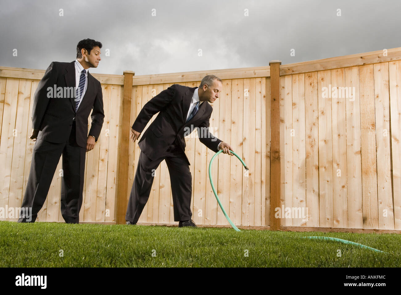 Low angle view of a businessman watering grass with another businessman ...