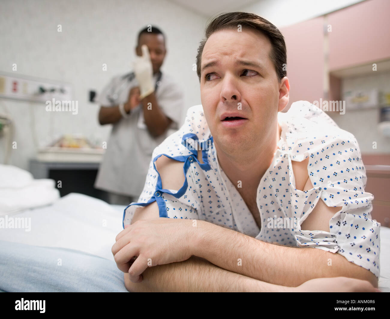 A nervous patient lying on the bed with a doctor putting on latex ...