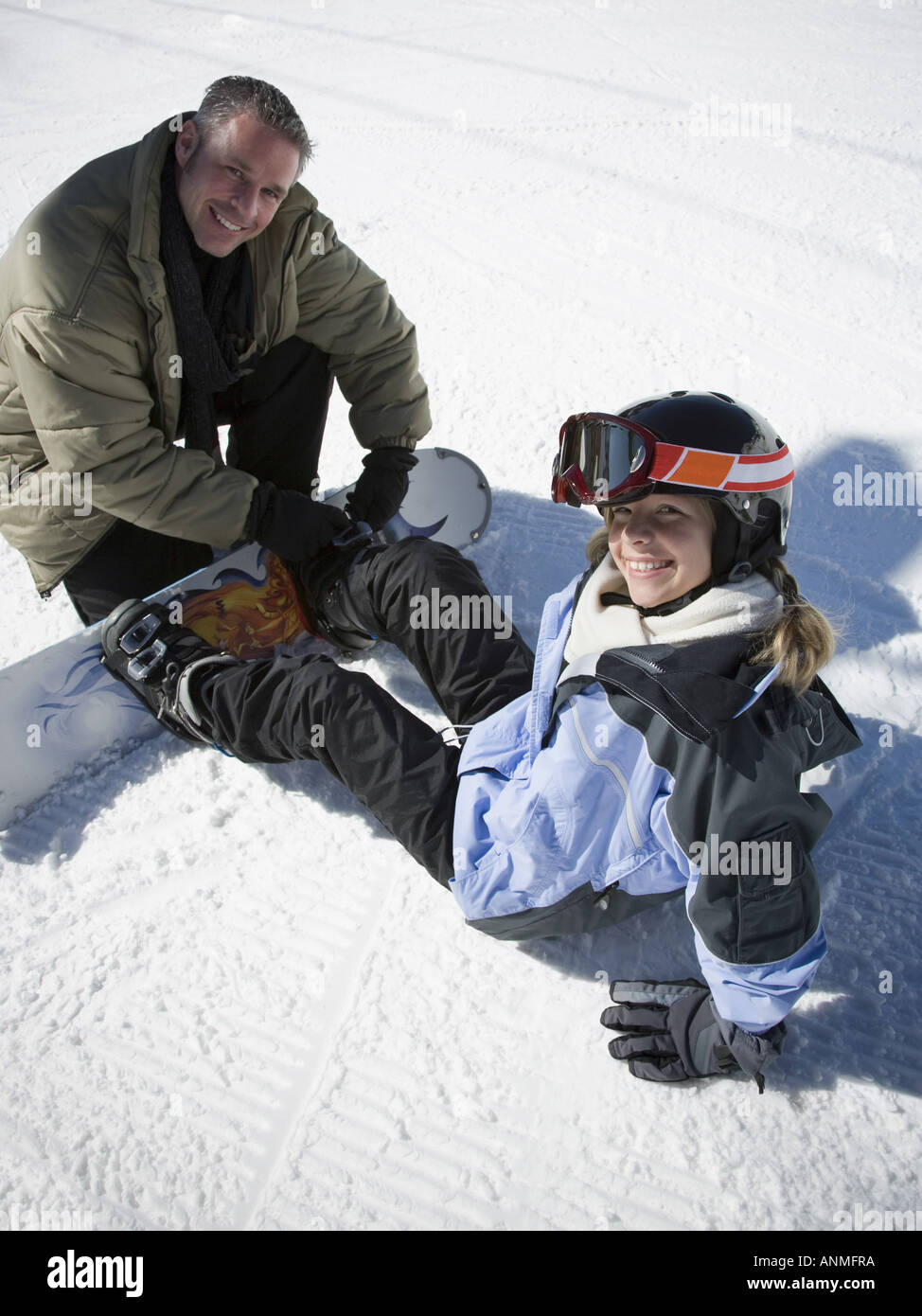 High angle view of a father helping his daughter put on a snowboard ...