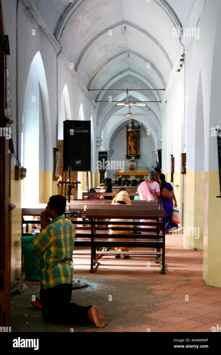 A man kneeling down in prayer against the background of a row of pews ...