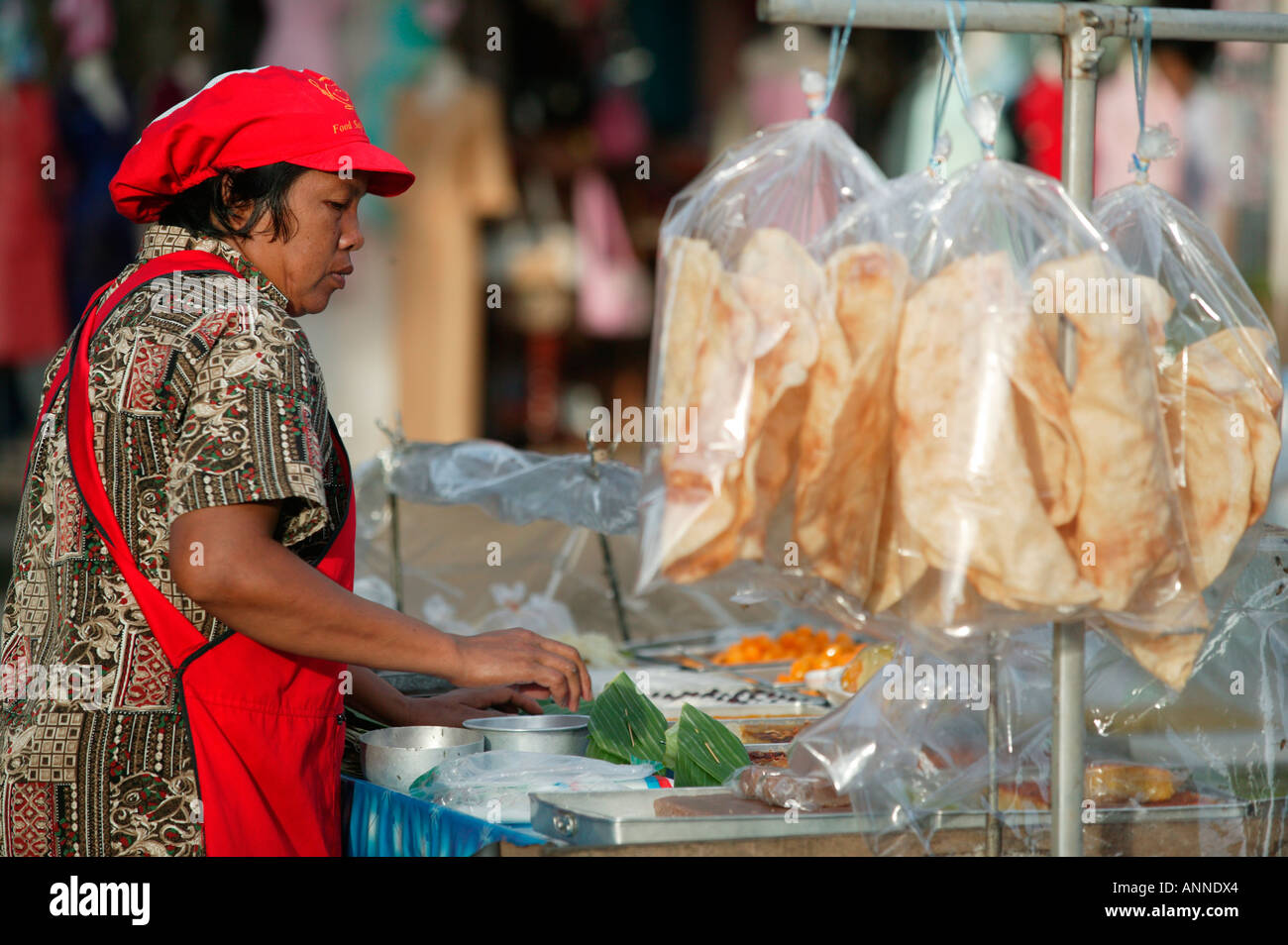 Woman market stall holder cooking food with popadoms hanging in bags on ...