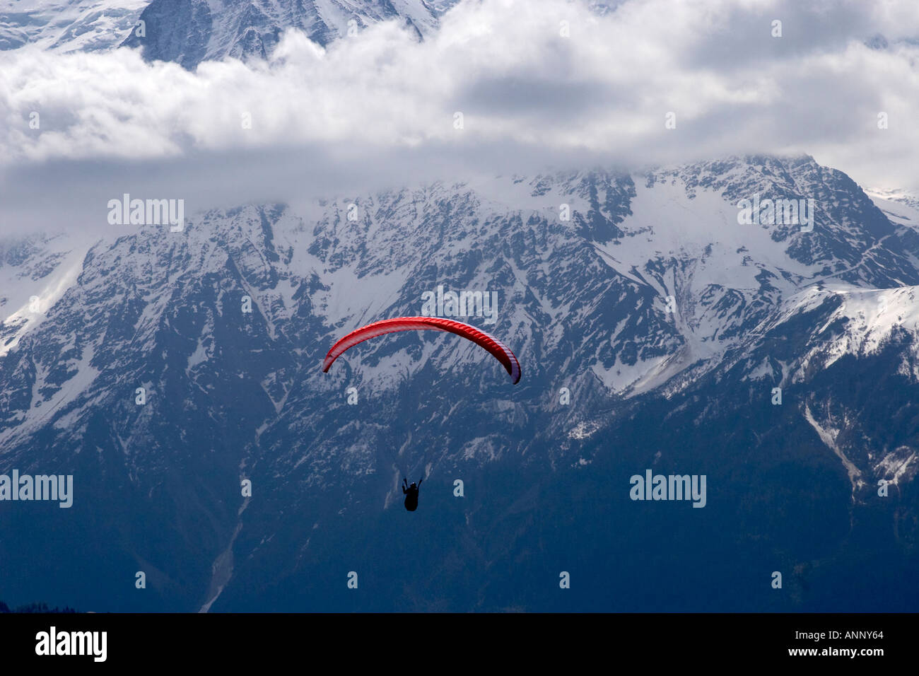Paragliding pilot flying red paraglider with snow covered peaks in ...