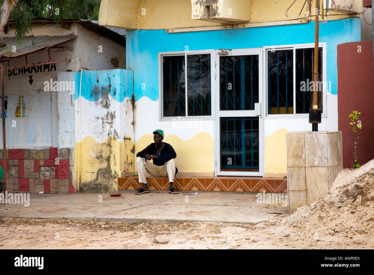 An African Gambian man sitting on a doorstep in a street in the Kololi ...