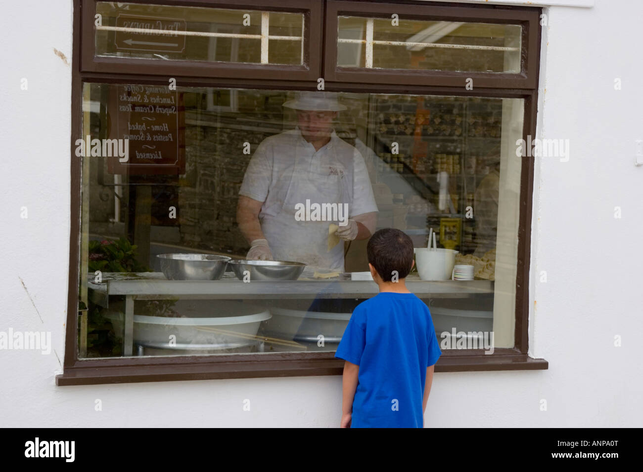 Little boy watching the baker prepare food behind the bakery window ...