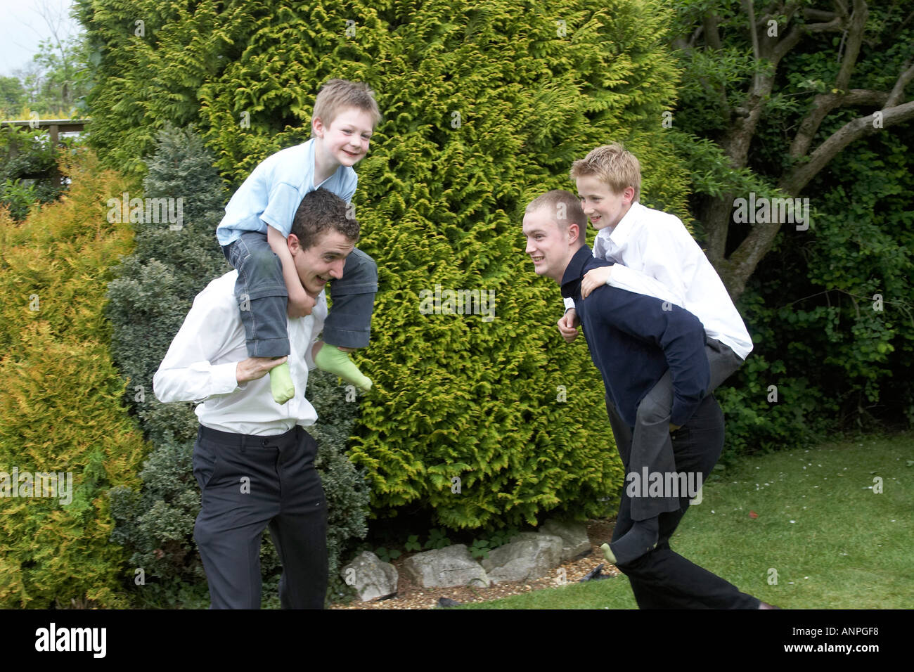Boys playing a piggyback fighting game outdoors in a garden England UK ...
