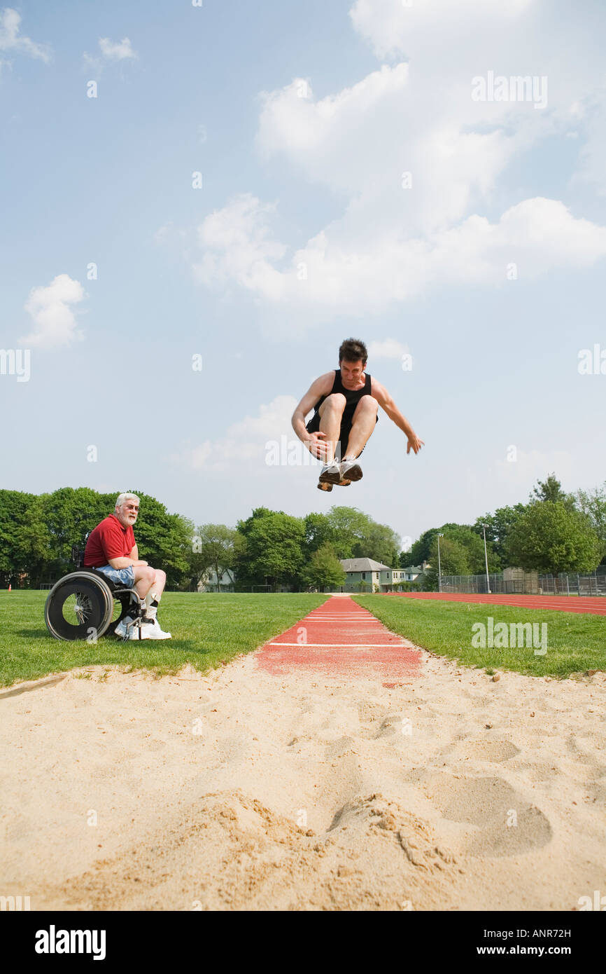Young man practicing long jump with a handicapped senior man watching ...