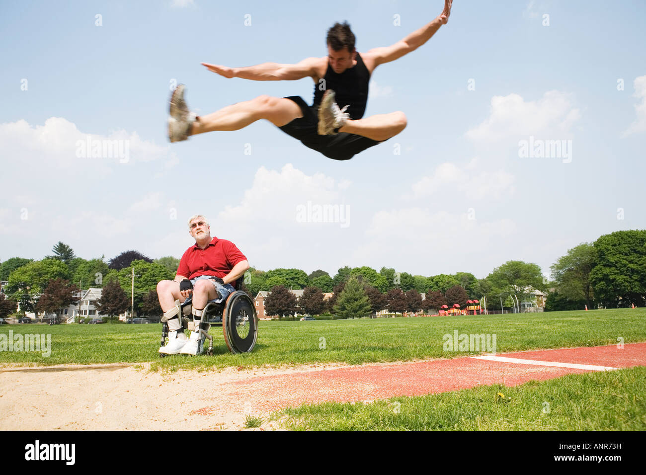 Young man practicing long jump with a handicapped senior man watching ...