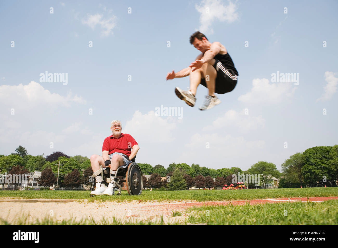 Mid adult man long jumping with a middle-aged man sitting in a ...