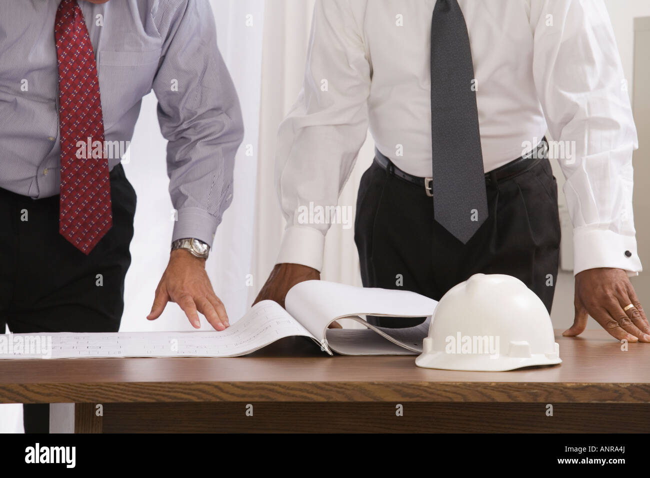 Mid section view of two engineers looking at a blueprint in an office ...