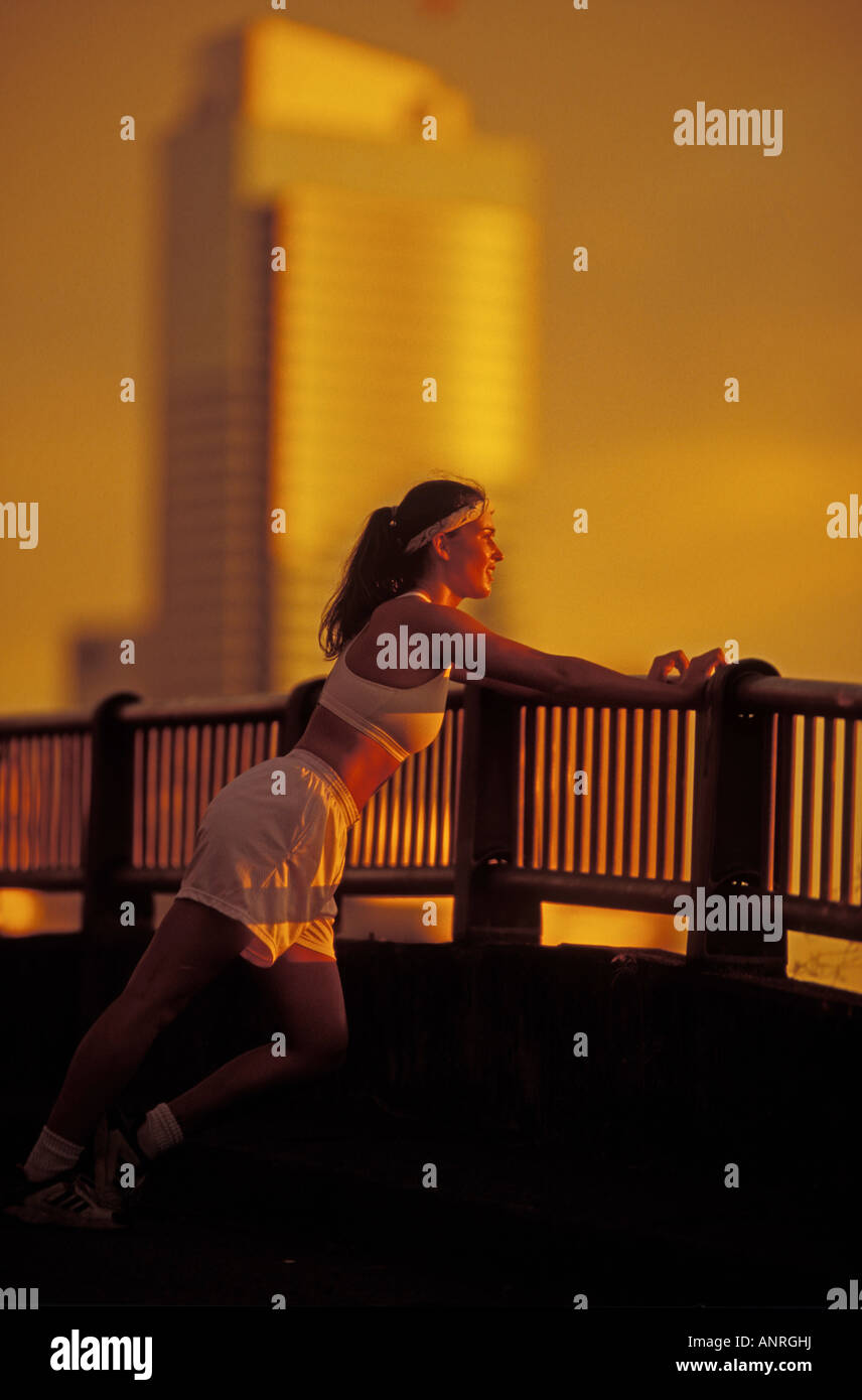 A woman runner stretches against a railing during a run at sunset Stock ...