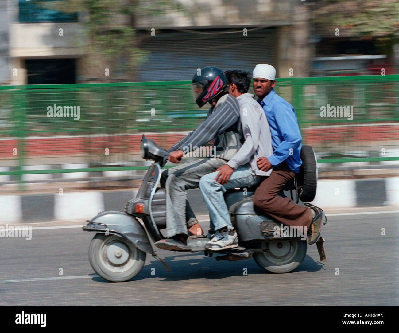 Three men travelling on a scooter on a motorway in India. Fast and at ...