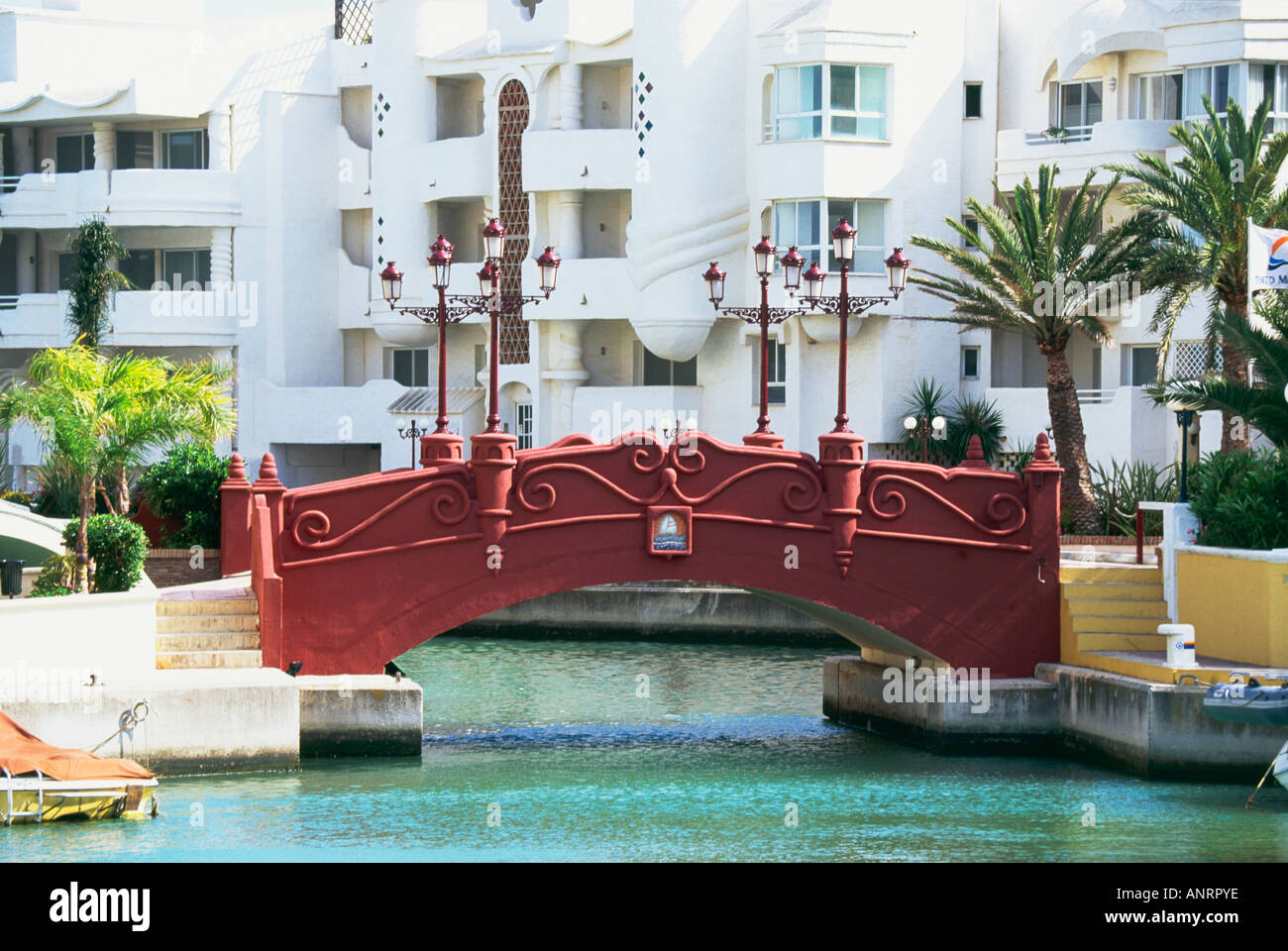 A small pink bridge bearing lamp posts crosses an inlet of water beside ...