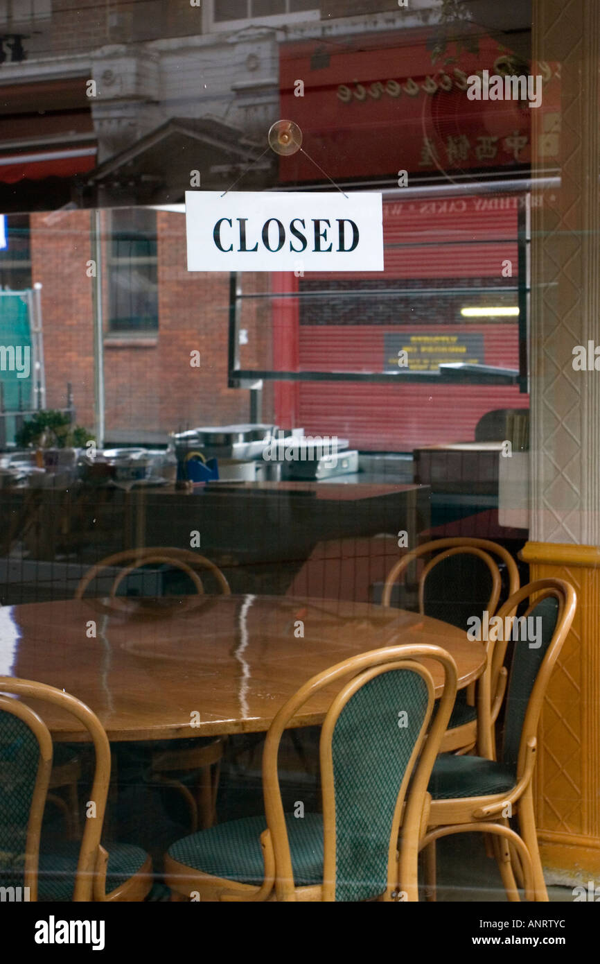 a closed sign on the window of a restaurant Empty tables are visible ...