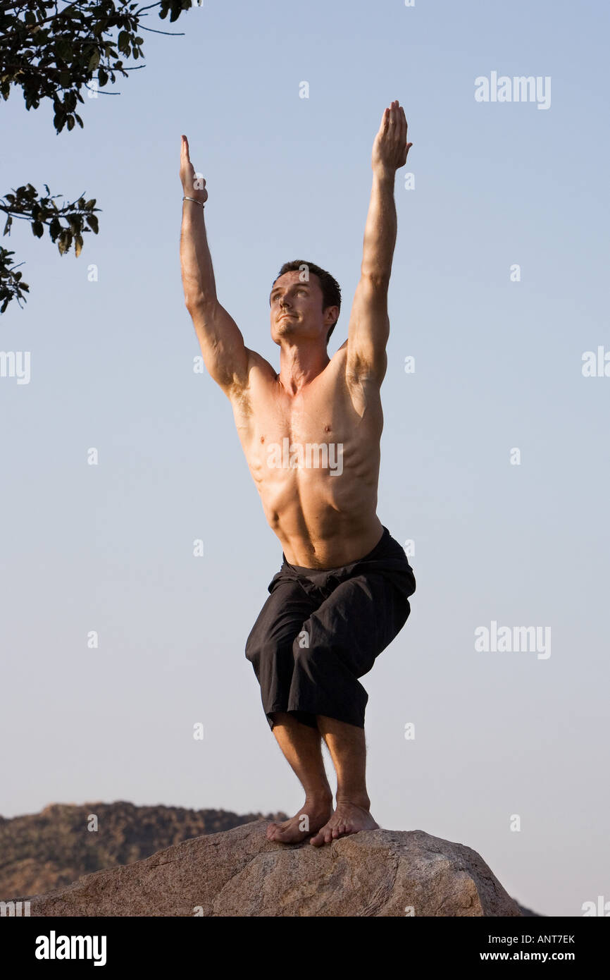 Man performing Hatha Yoga utkatasana Chair Pose on a rock in India ...