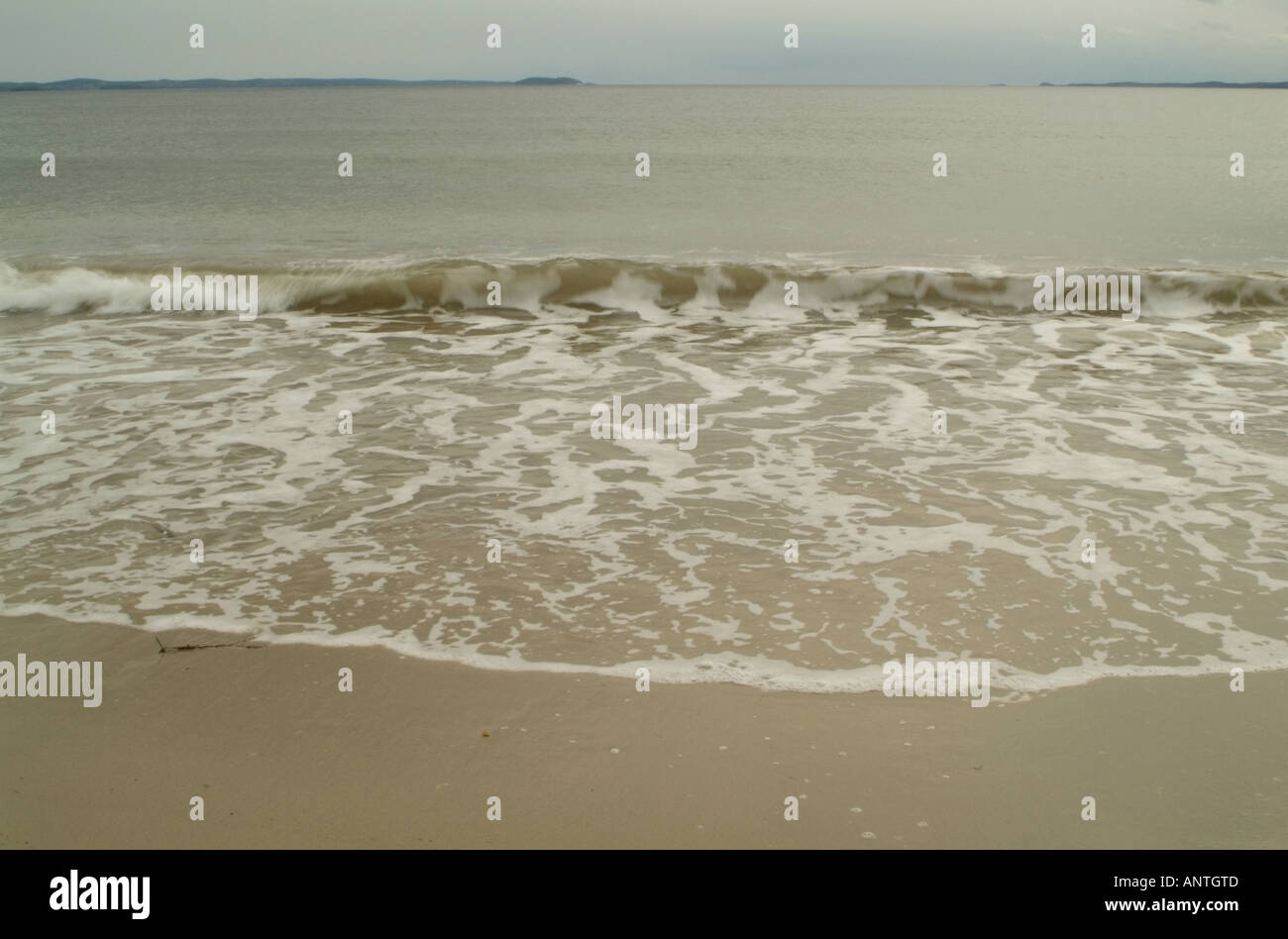 A wave slowly rolls in over perfectly smooth sand. The horizon is ...