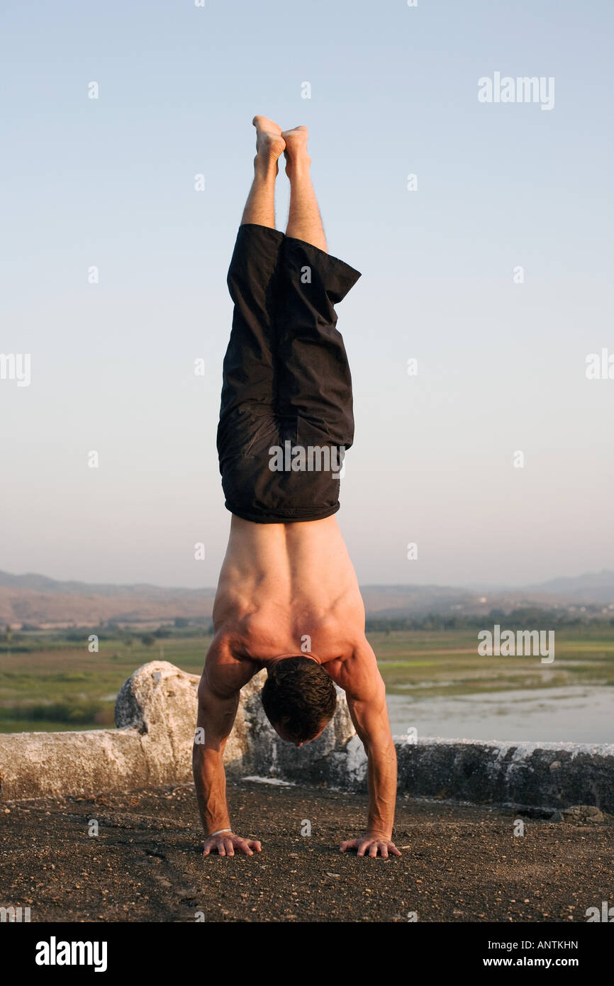 Man performing Hatha Yoga hand stand pose on a hindu temple in India ...