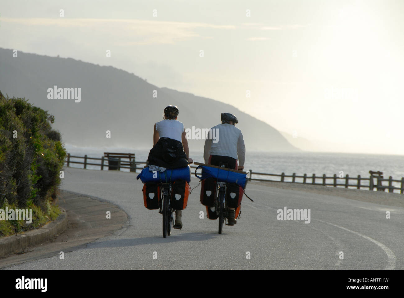 Two cyclists with heavy loads on bicycles riding along seashore in ...