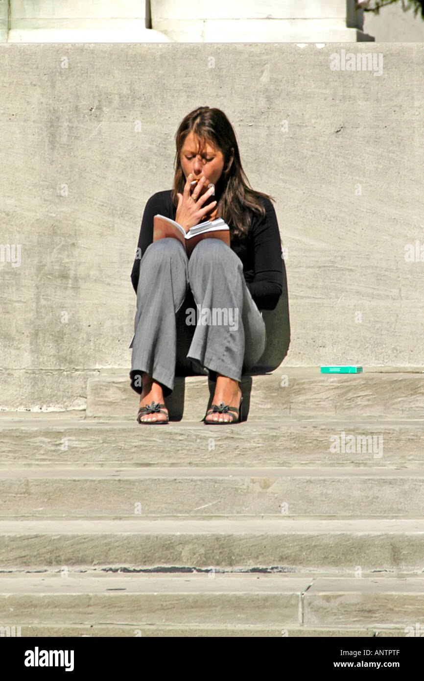 Adult Female smoking a cigarette and reading a book during her lunch ...