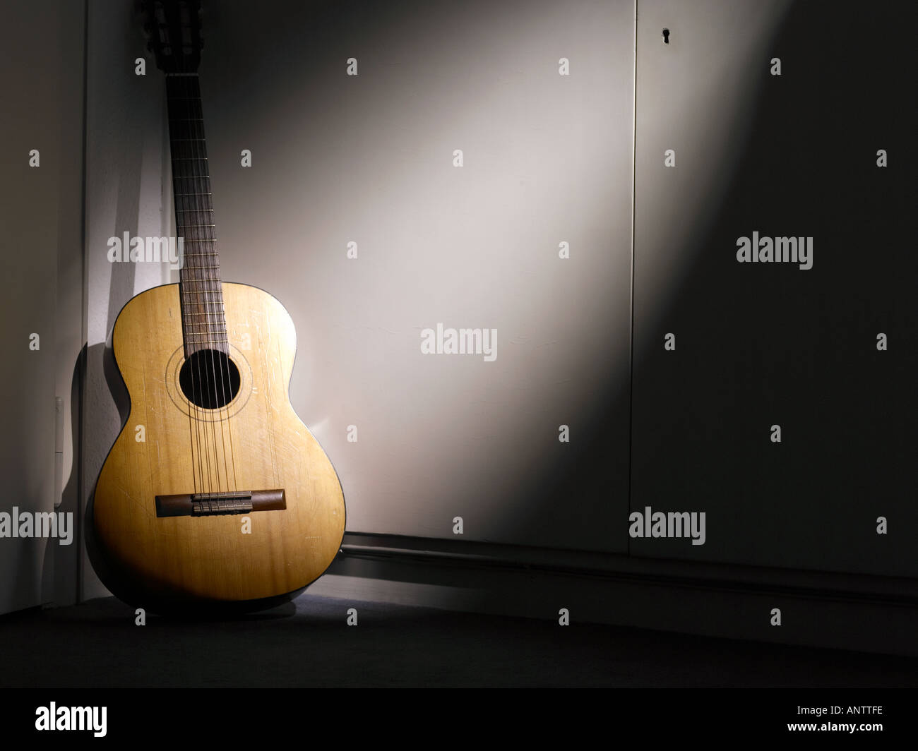 Scratched acoustic guitar leaning in corner of room Stock Photo - Alamy