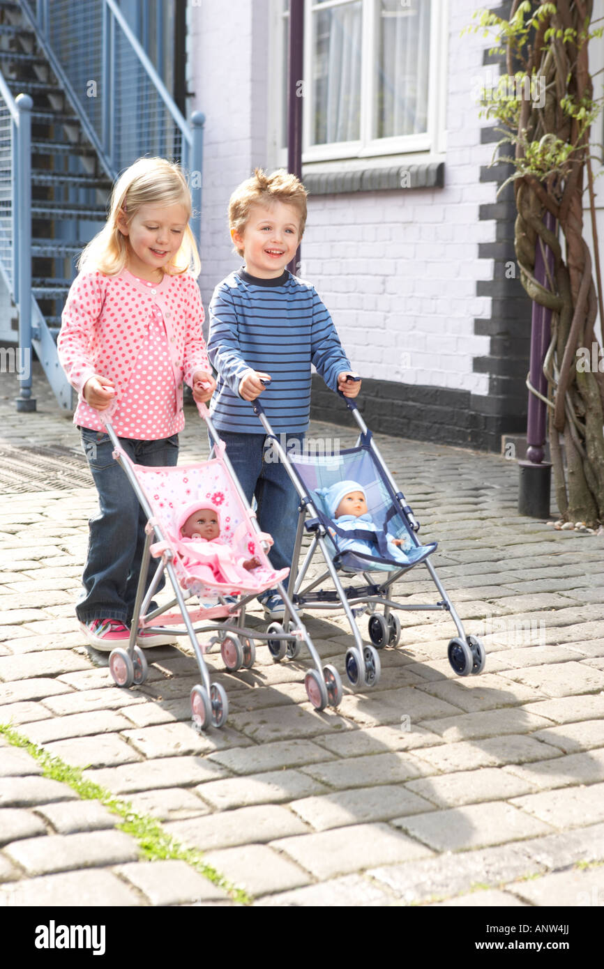 a boy and a girl push dolls in toy push chairs outside on a cobbled ...