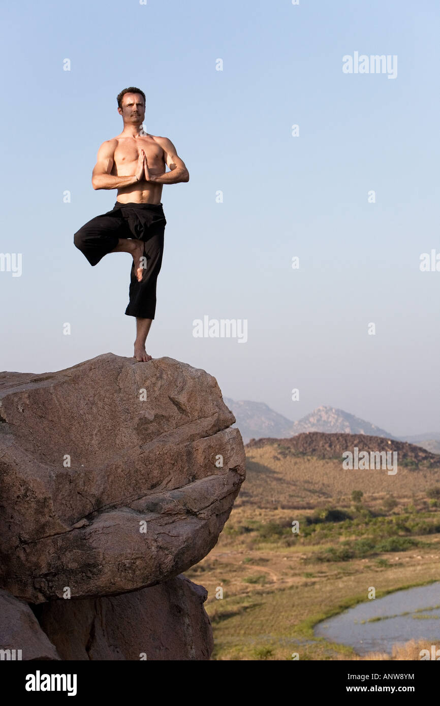 Man performing Hatha Yoga, vrikhasana, tree pose on a rock in India ...