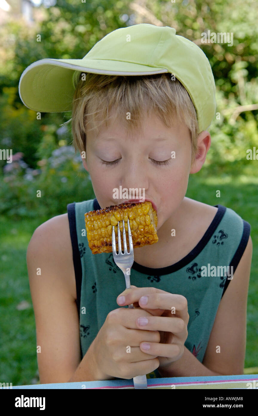 Boy, eleven-year-old, is eating fried or grilled maize corn with ...