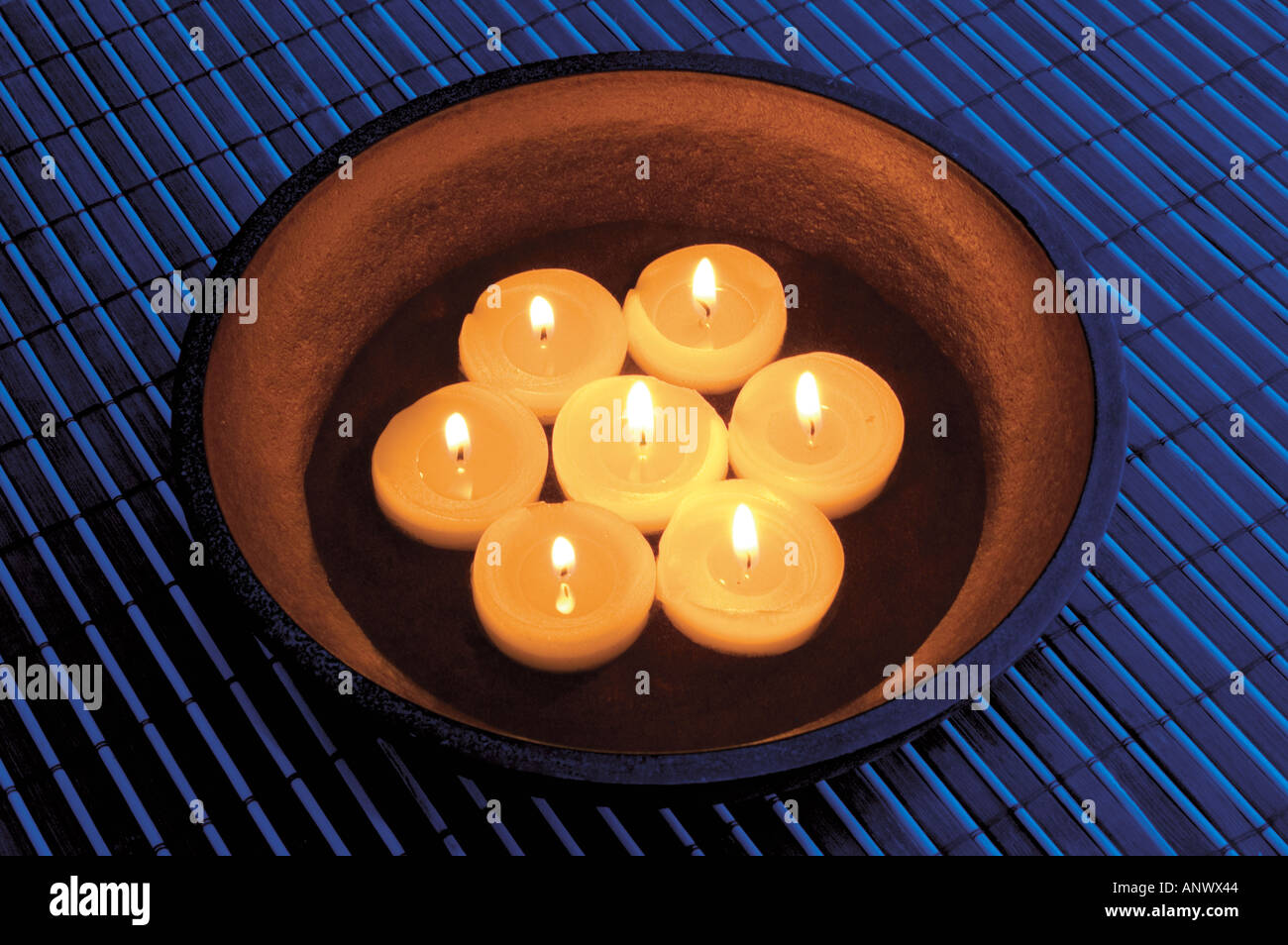 wooden bowl containing several small tealight candles lit on japanese ...