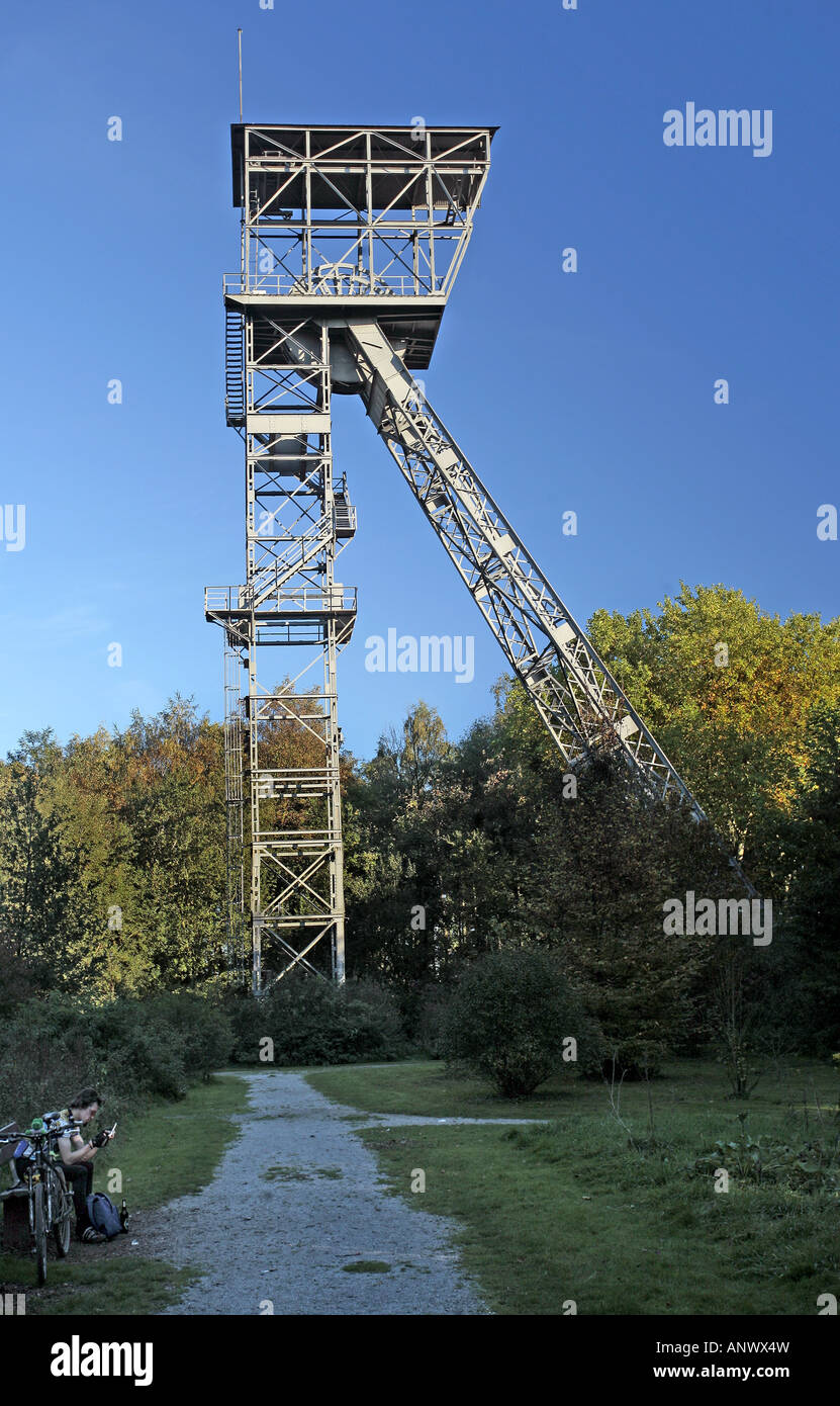 man sitting on a park bench in front of the headgear of the former coal ...